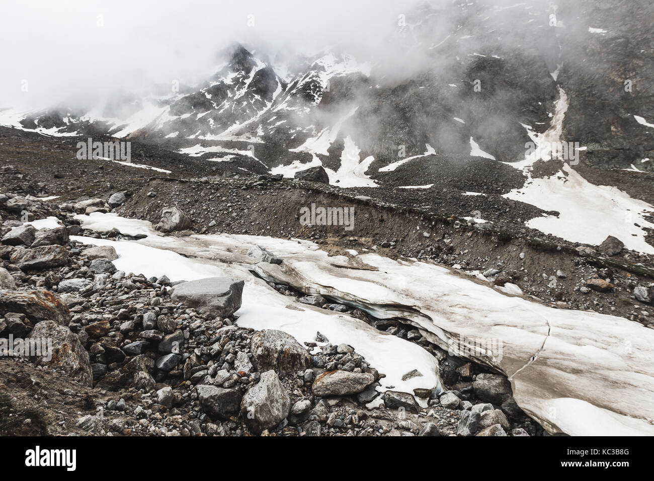 Mountain landscape with rocks and creeping fog. High snow peaks in the ...