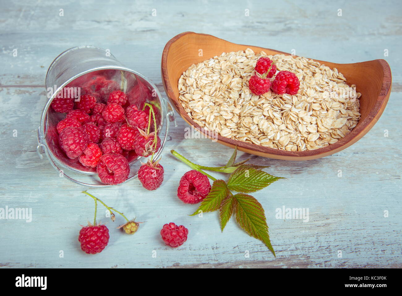 Fresh raspberries in a bucket and oat flakes in a wooden bowl on a ...