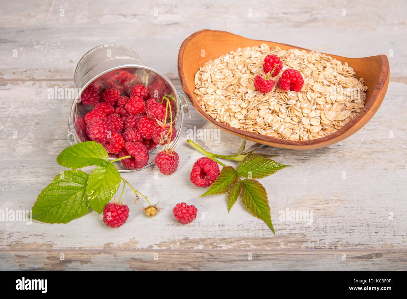 Fresh raspberries in a bucket and oat flakes in a wooden bowl on a ...