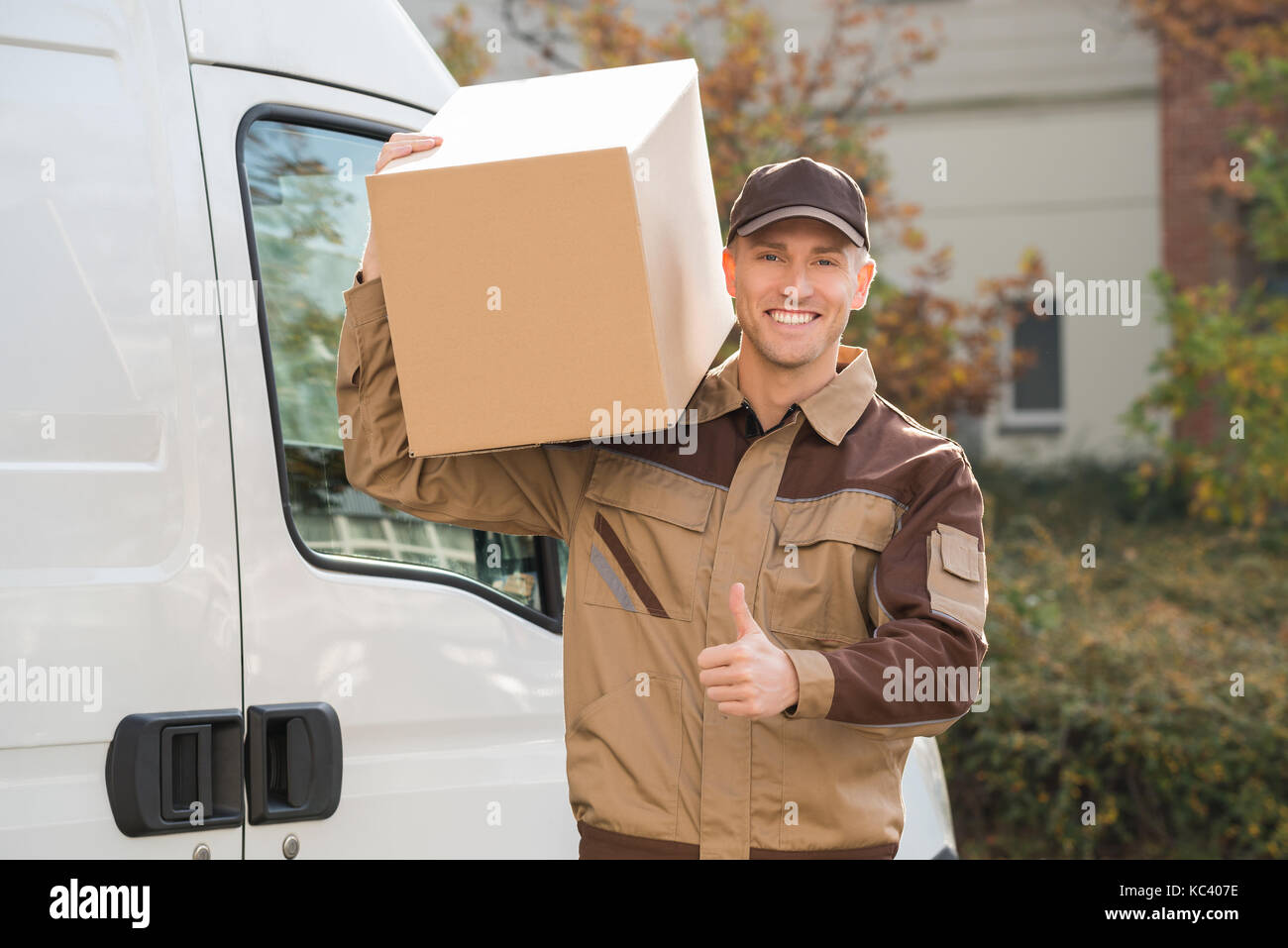 Portrait of young delivery man carrying cardboard box on shoulder with ...