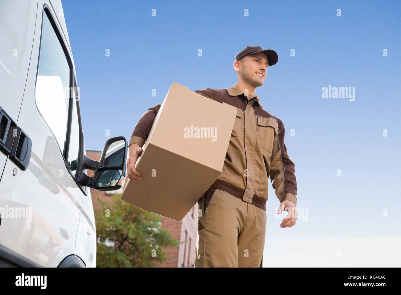 Low angle portrait of young delivery man carrying cardboard box against ...
