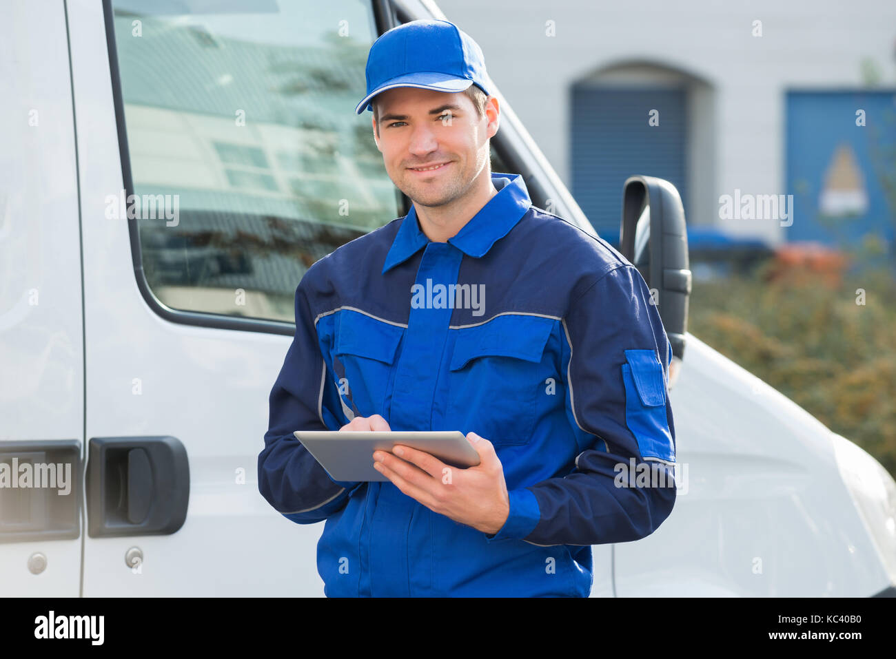 Portrait of delivery man smiling using digital tablet by truck Stock ...