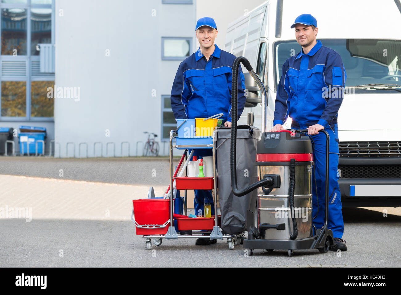 Portrait of confident male janitors with cleaning equipment standing on ...