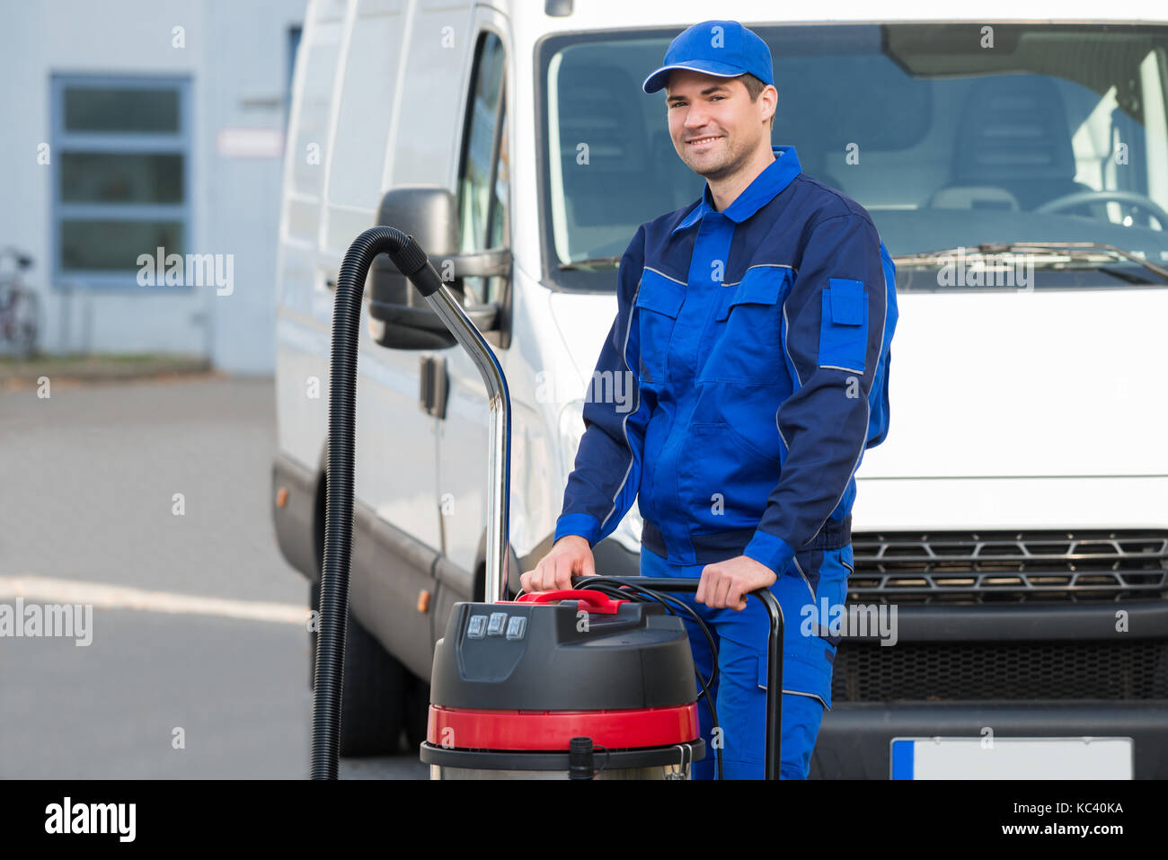 Portrait of confident male janitor standing with vacuum cleaner on ...