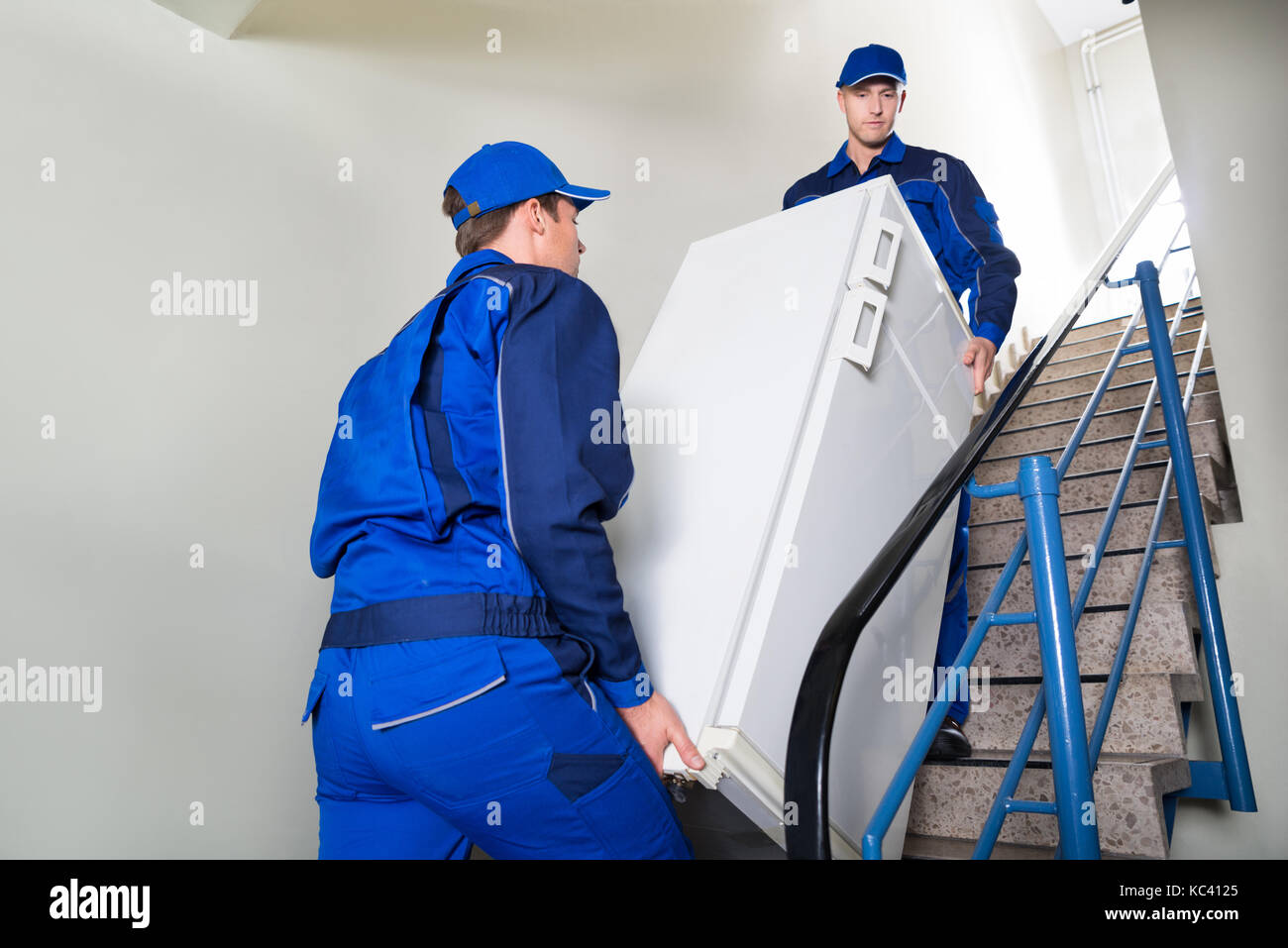 Side view of movers carrying refrigerator while climbing steps at home ...
