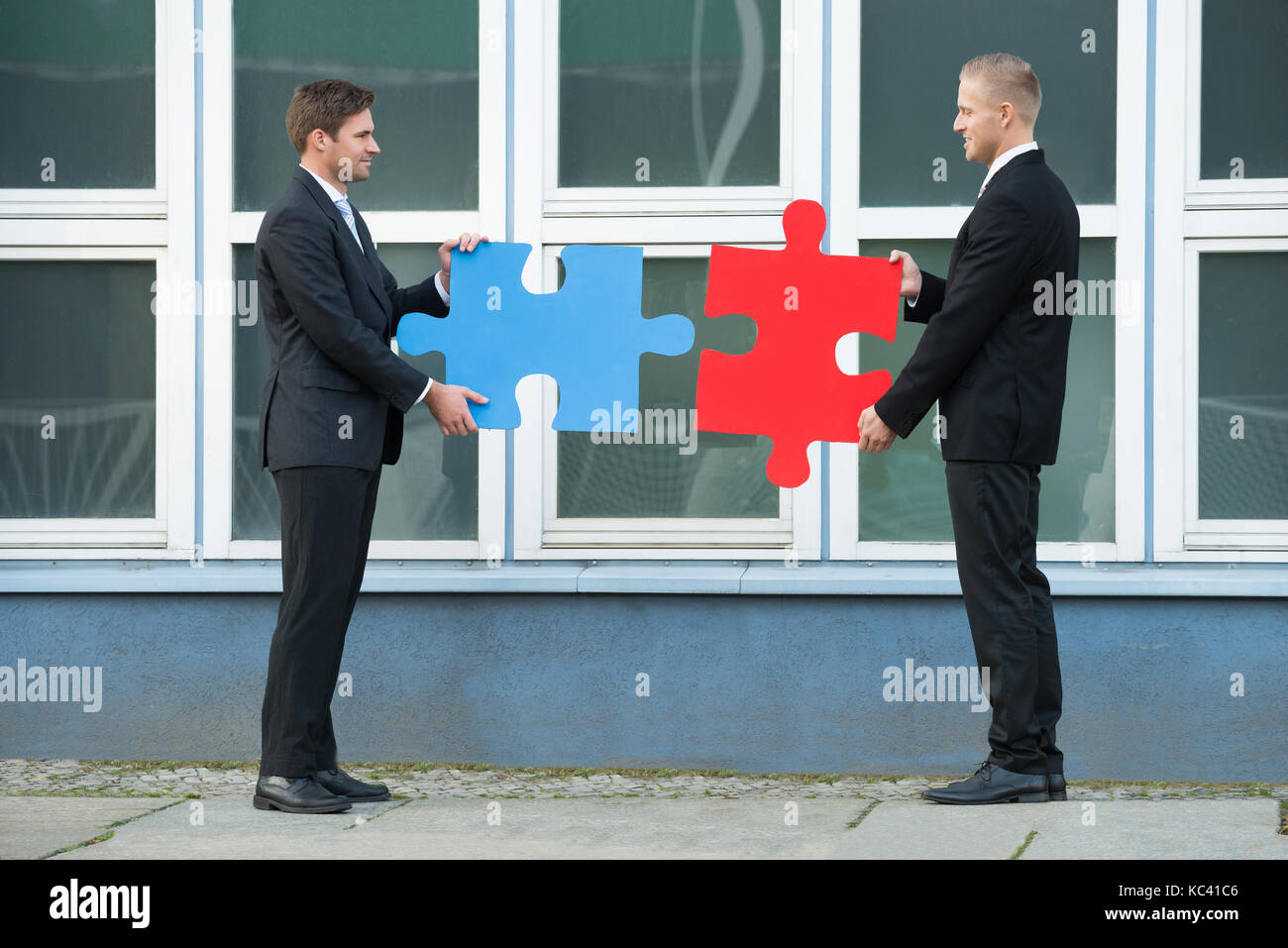 Side view of businessmen joining jigsaw pieces while standing outside ...