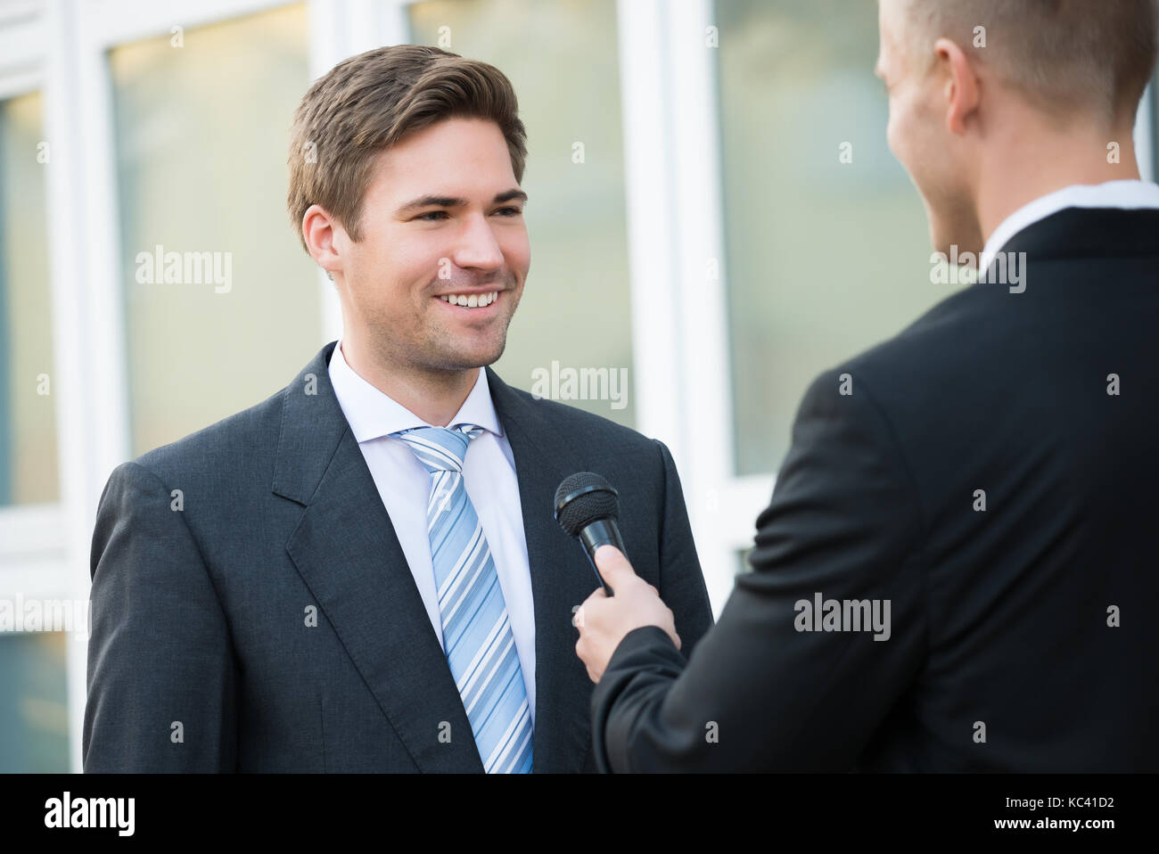 Rear view of male journalist taking interview of happy businessman ...
