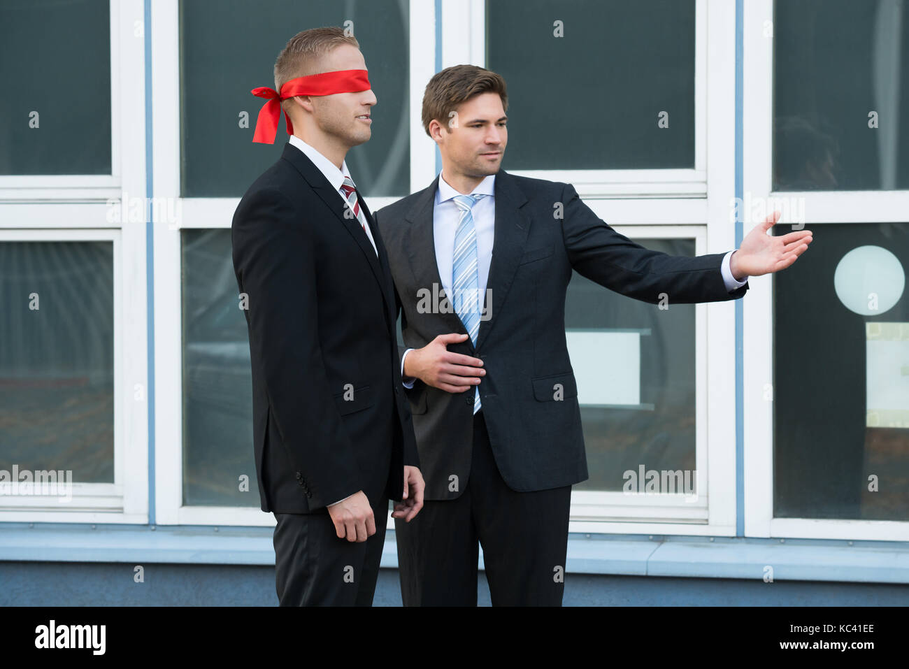 Confident young businessman assisting blindfolded partner outside ...