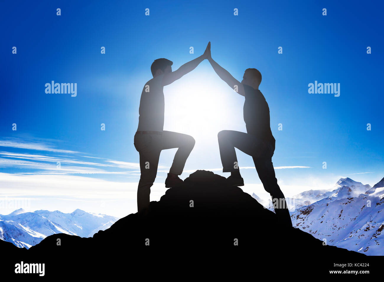 Side view of silhouette male friends giving high five on mountain peak ...