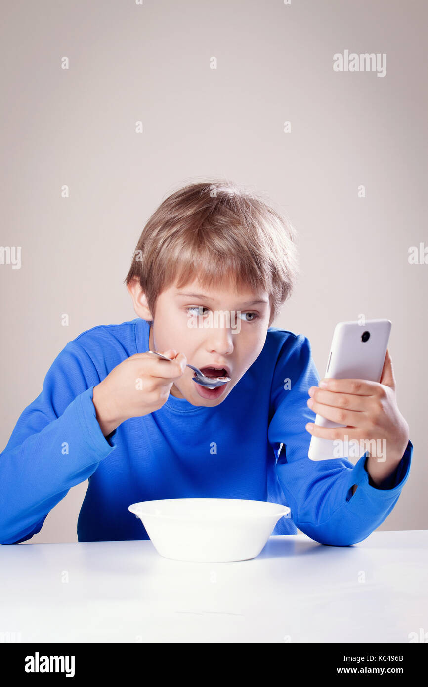 Kid eating breakfast whilst using mobile phone Stock Photo - Alamy
