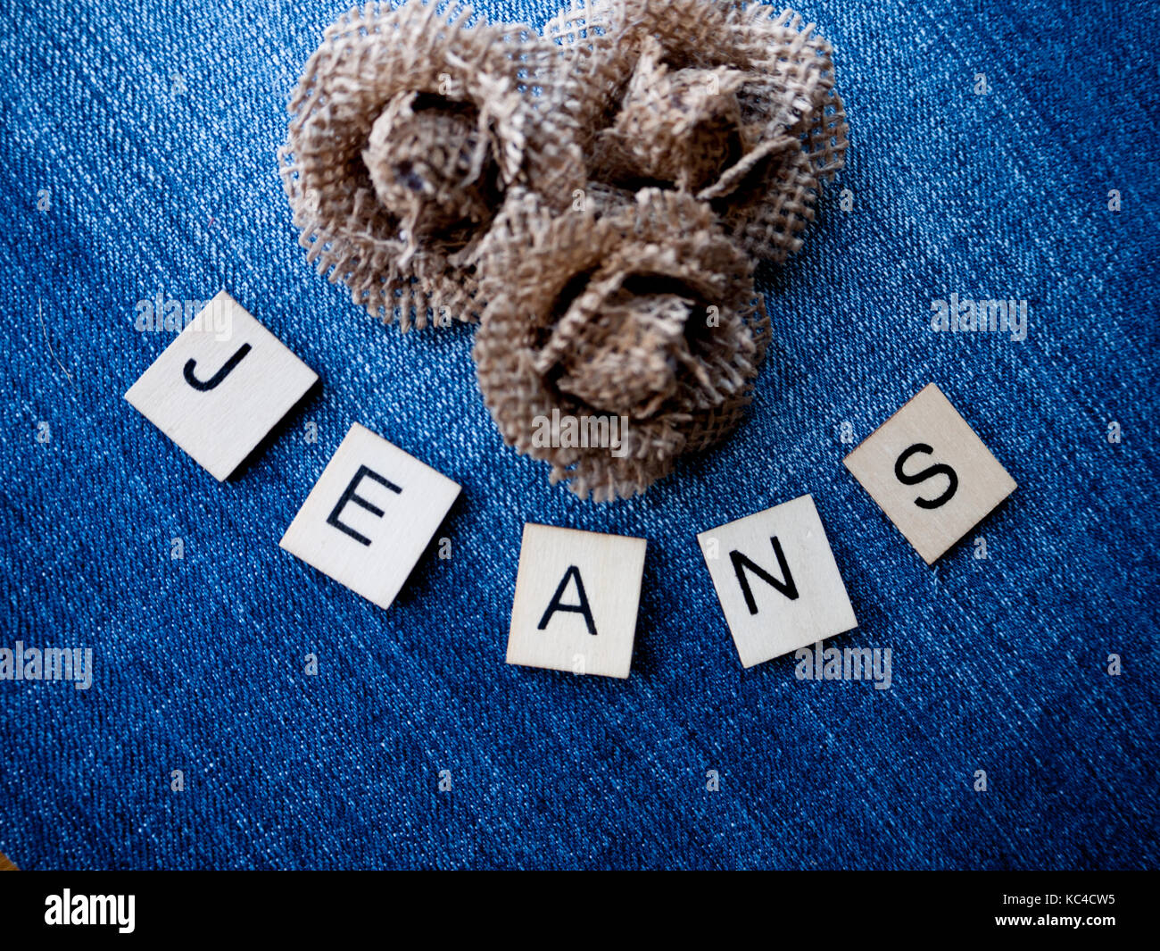 The word "Jeans" spelled out with wooden letter tiles on denim fabric ...