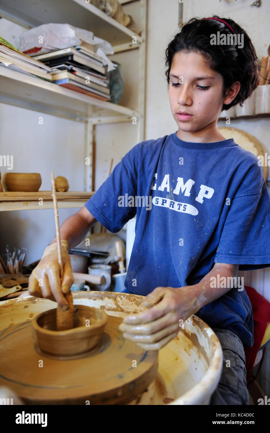 Germany, boy learning pottery, making pots from clay at turning wheel ...