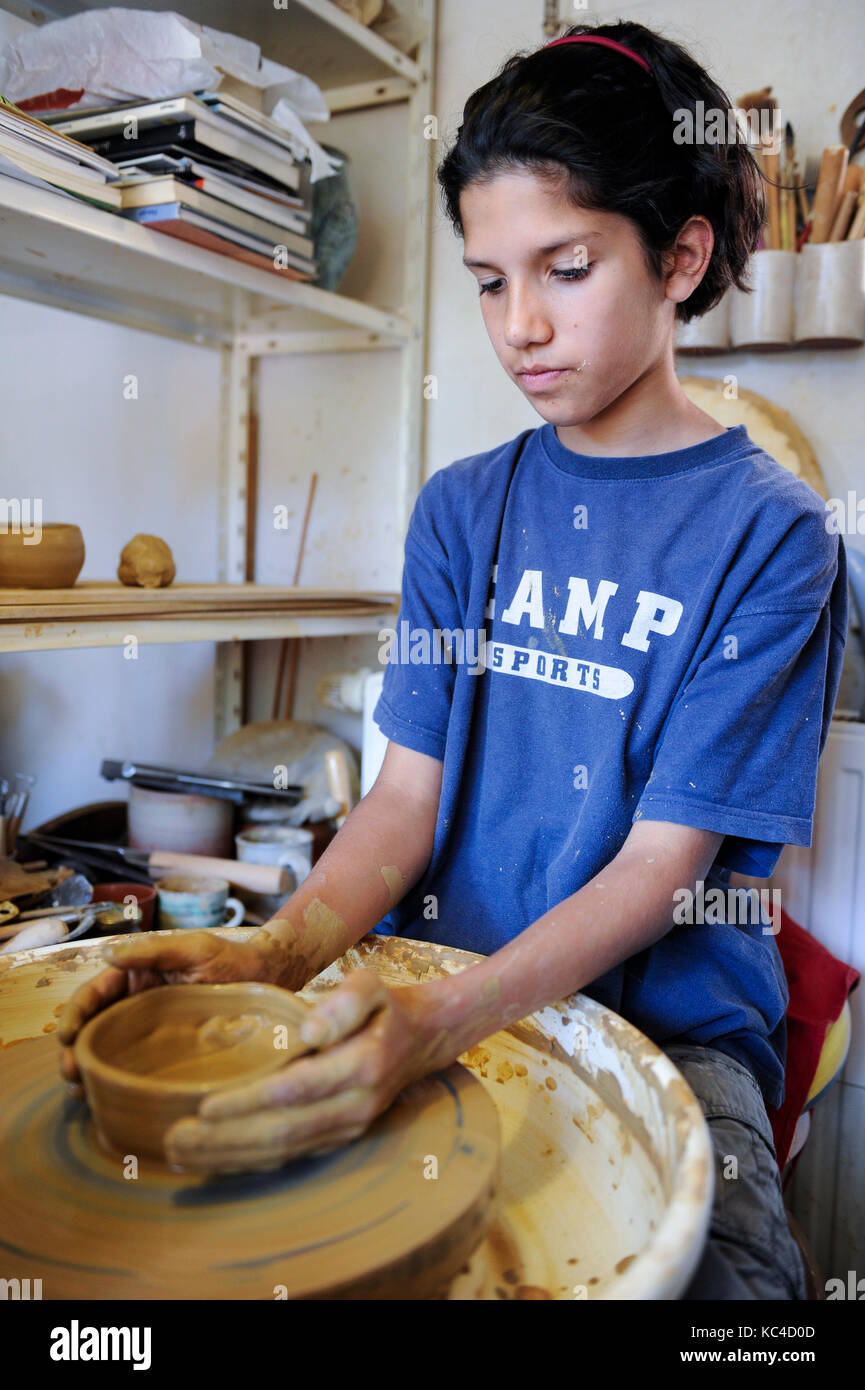 Germany, boy learning pottery, making pots from clay at turning wheel ...