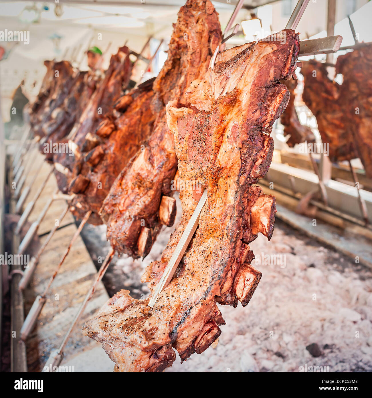 Roasted meat of beef cooked on a vertical grills placed around fire ...