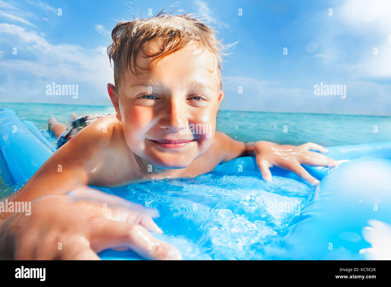 Boy swim in the water smiling on the blue matrass close portrait in ...