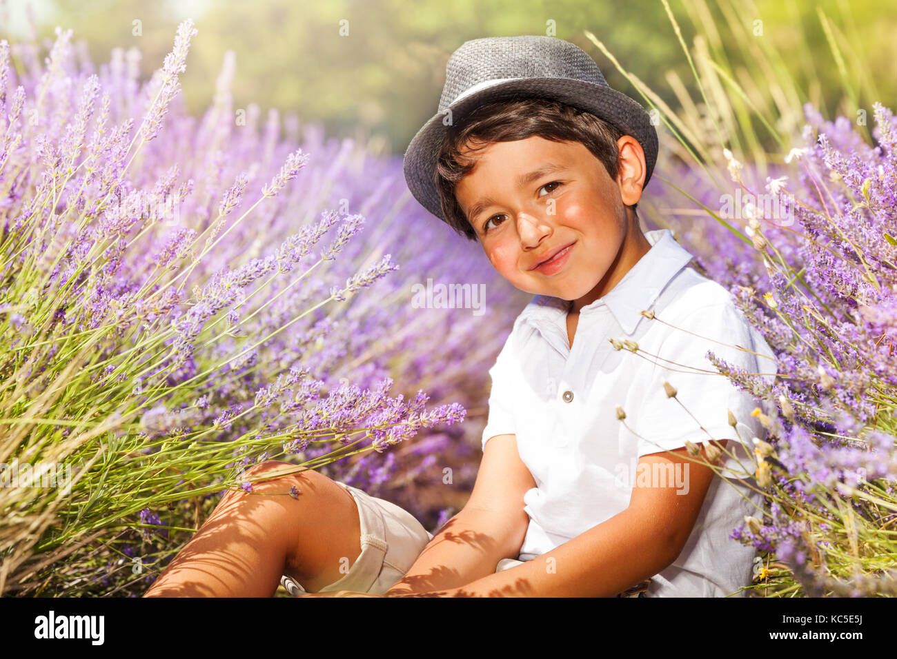 Close-up portrait of schoolboy in hat, sitting on the ground in ...