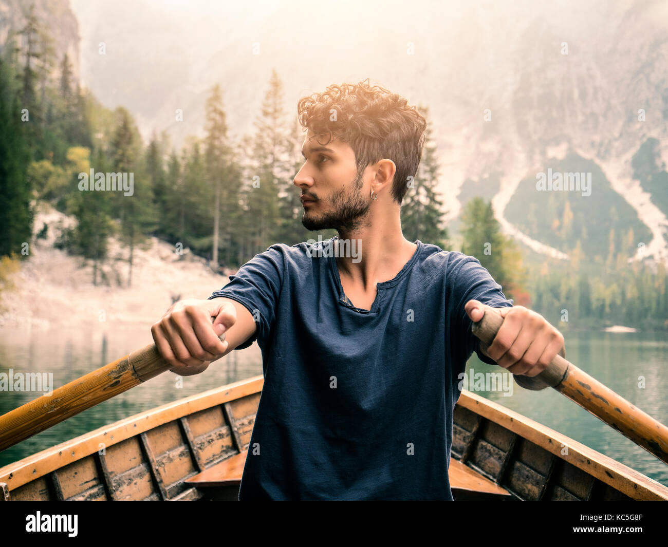 Young casual man sitting in boat and rowing while looking away on ...