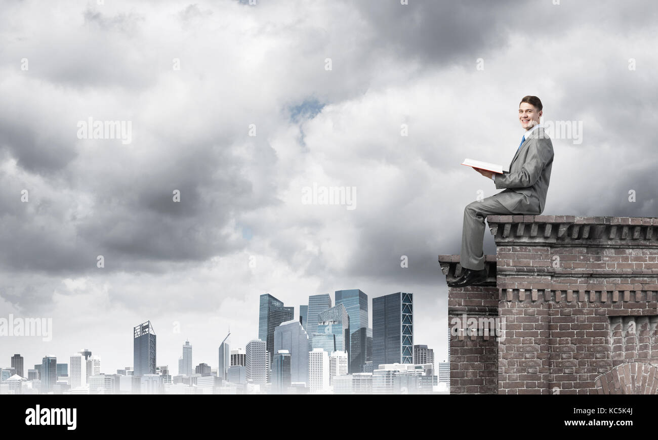 Man on roof edge reading book and cityscape at background Stock Photo ...