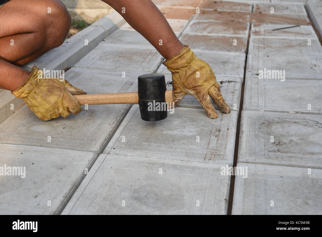Man with a rubber mallet taps tiles on a pathway as part of a DIY ...