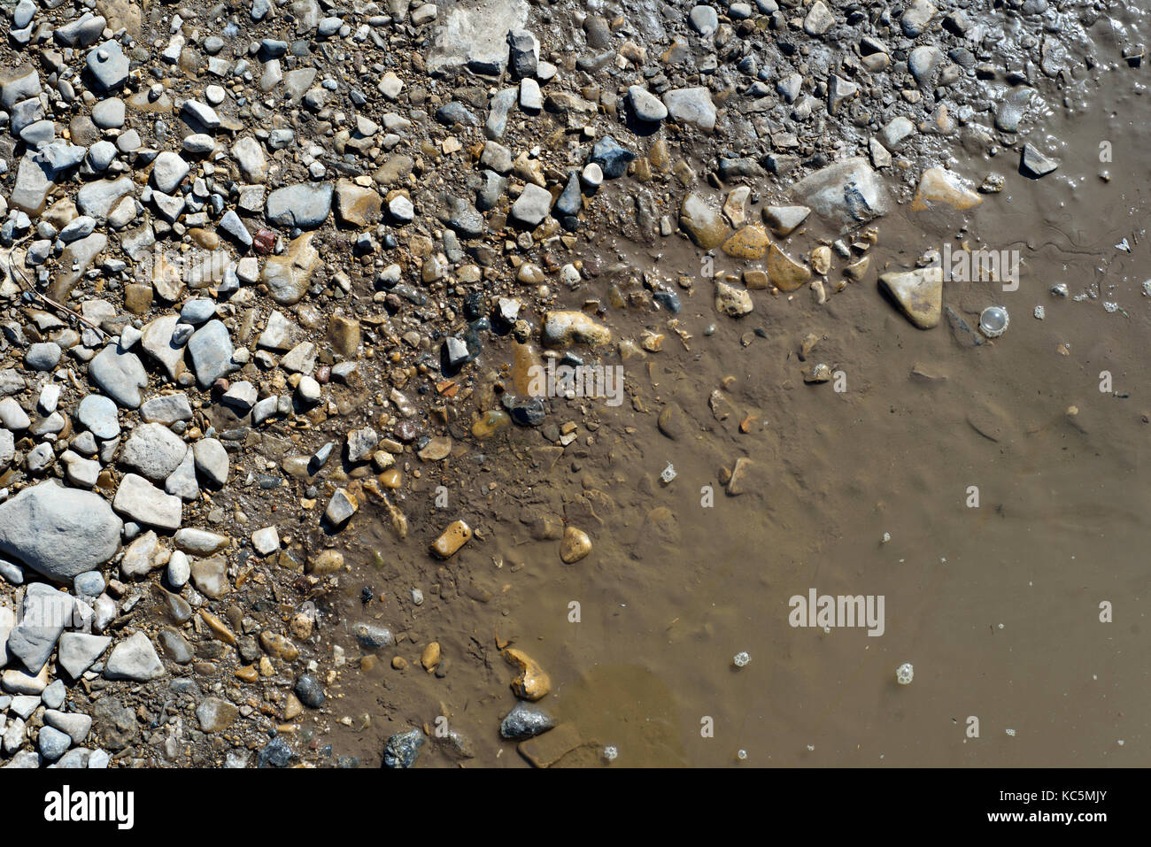 Murky dirty water from a muddy puddle recedes from the edge of stone ...