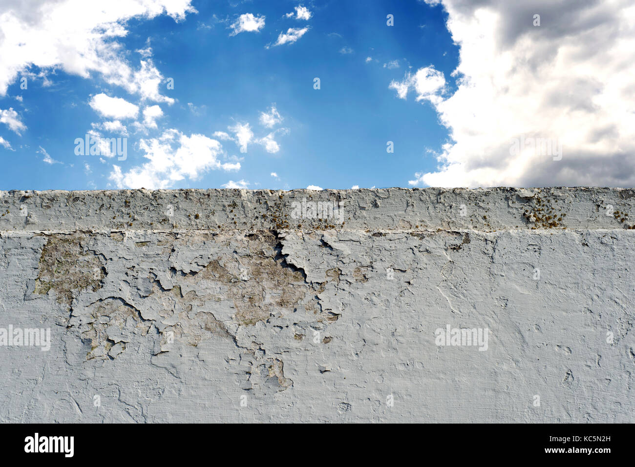 Crumbling white brick cement wall with flaking paintwork and a blue sky ...