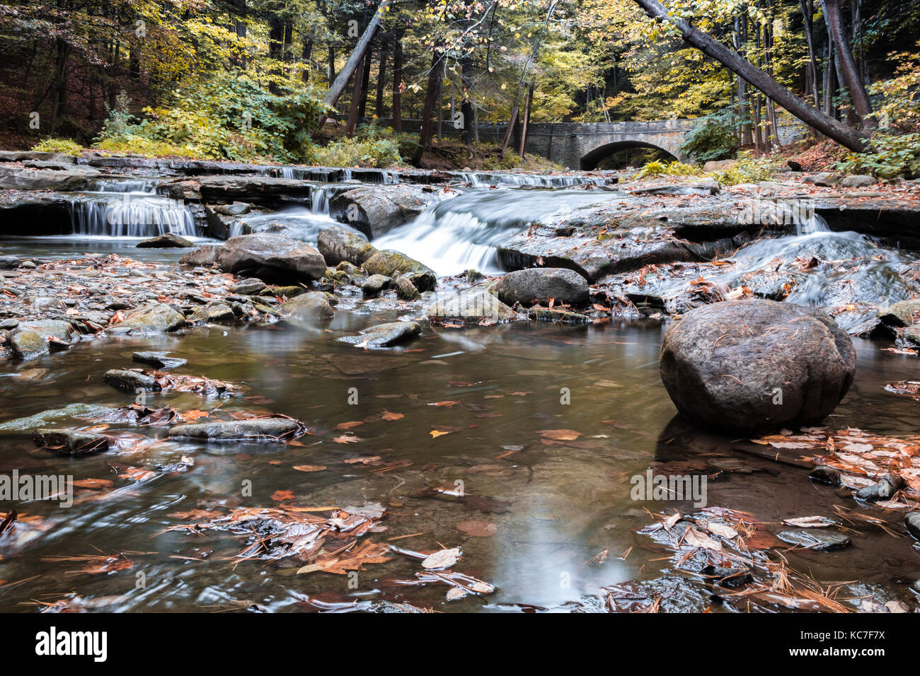 Graceful waterfalls flow around a stone walkway and curved bridge at ...