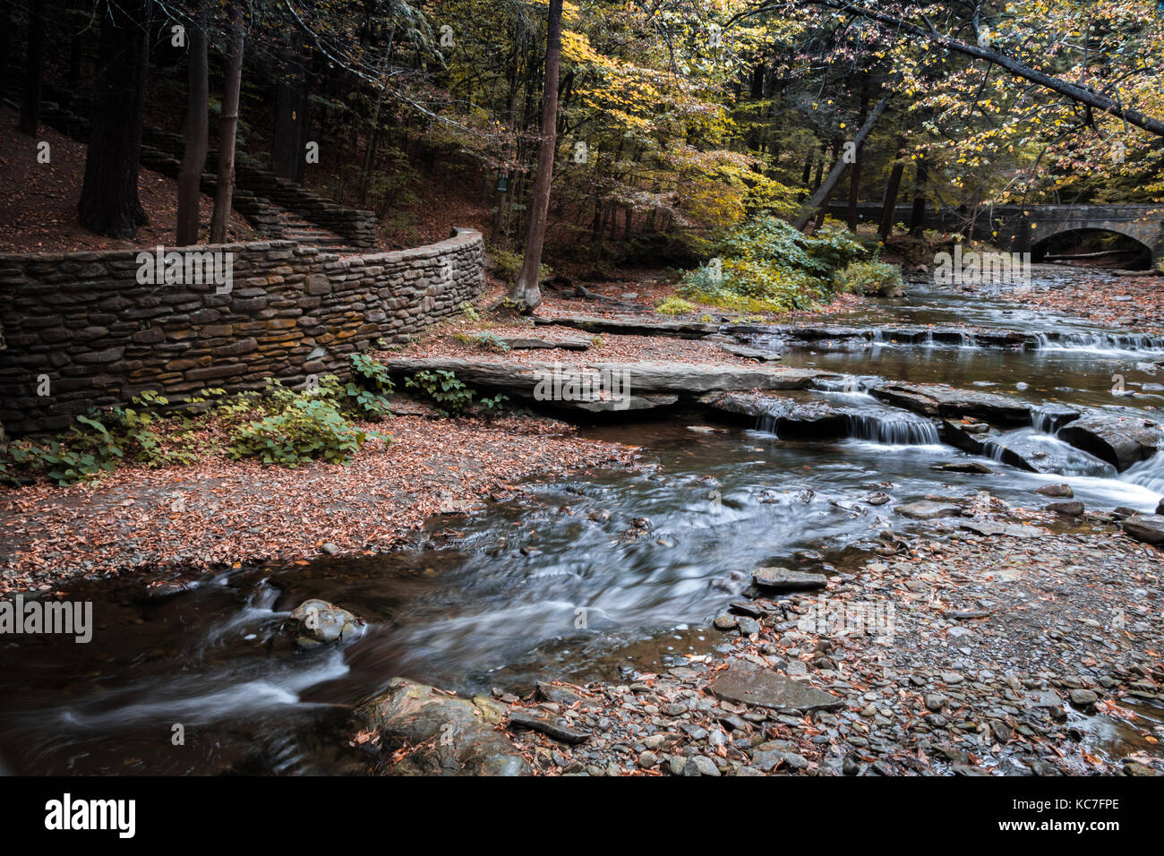 Graceful waterfalls flow around a stone walkway and curved bridge at ...