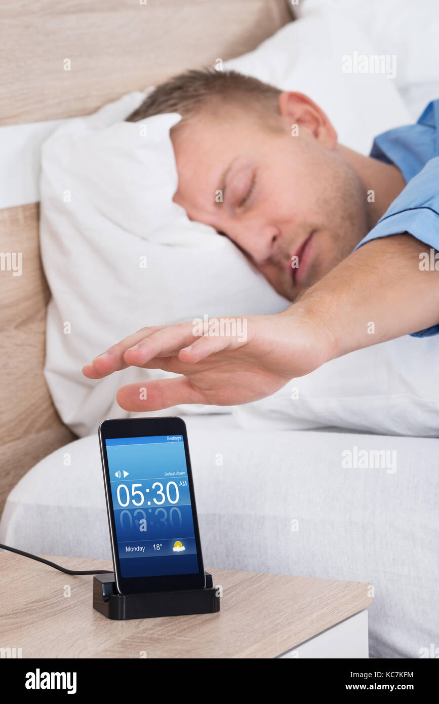 Man Lying On Bed Snoozing Alarm On Mobile Phone Screen Stock Photo - Alamy