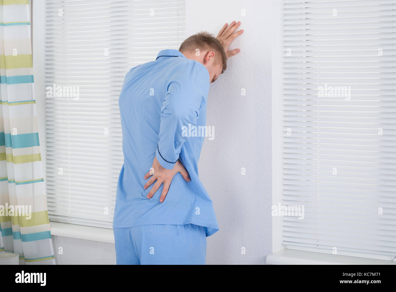 Man Suffering From Back Ache Standing Against Wall Stock Photo - Alamy