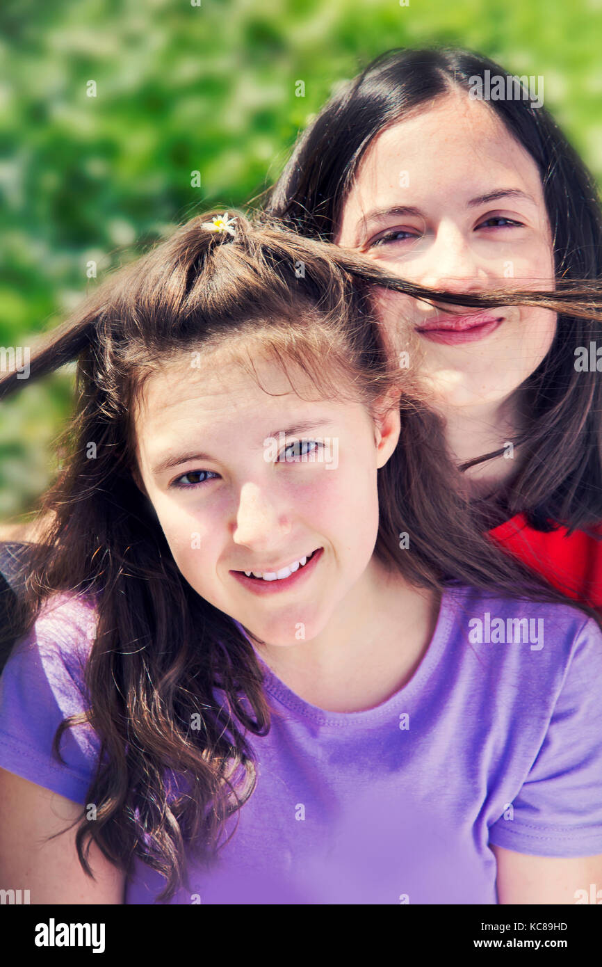 Portraits of two pretty teenage girls. Playing with her sisters hair ...