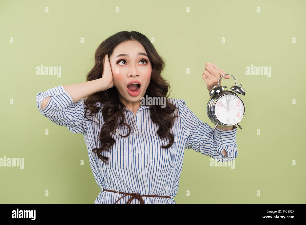 Surprised business woman holding alarm clock over green background ...