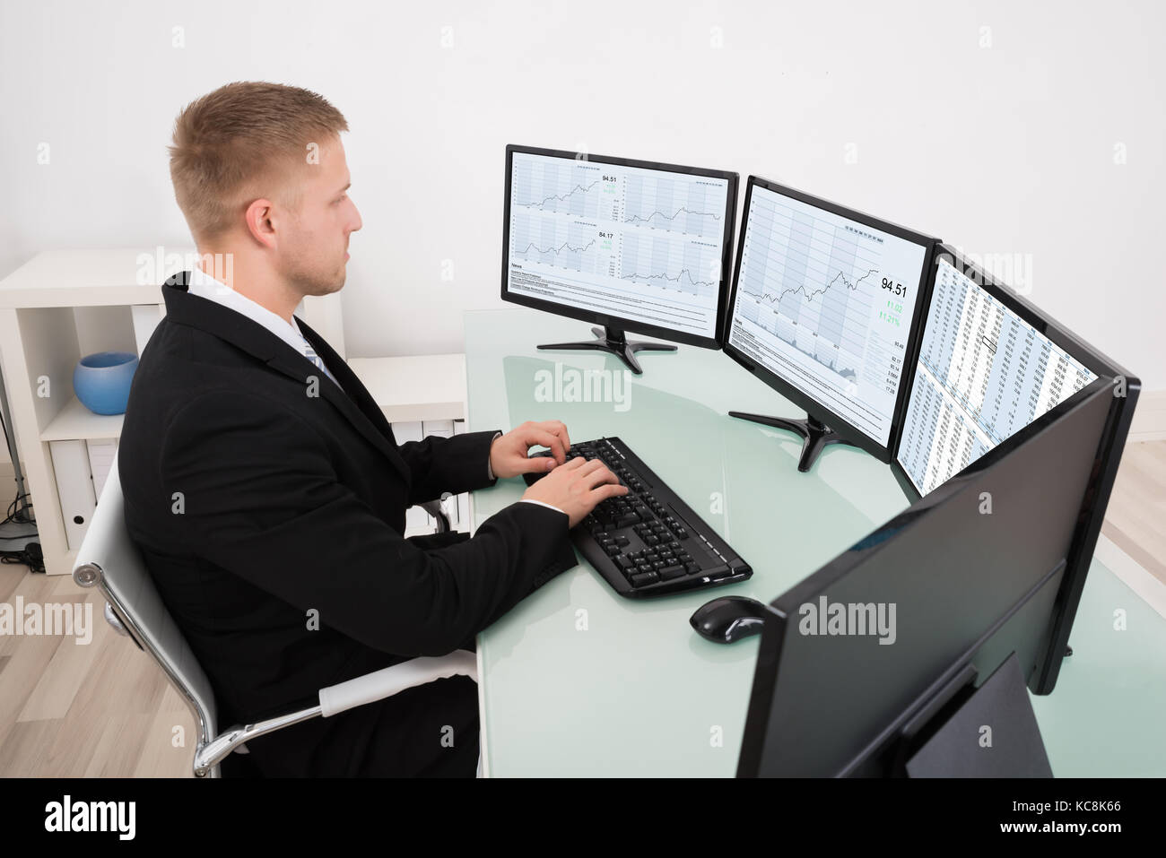 Young Businessman Looking At Graph On Multiple Computer Screen Stock ...