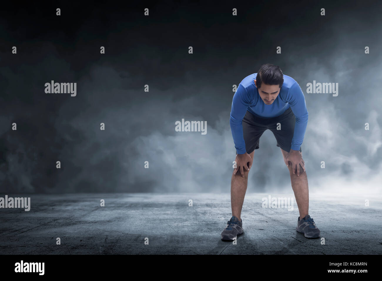 Young asian runner man taking rest from jogging on the concrete floor ...