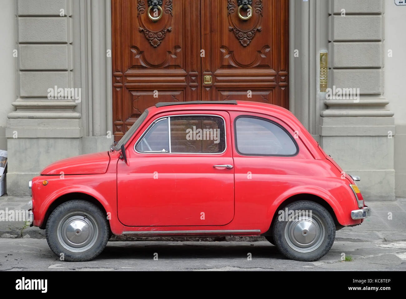 Red Fiat 500 parked on the street in front of an old brown wood ...