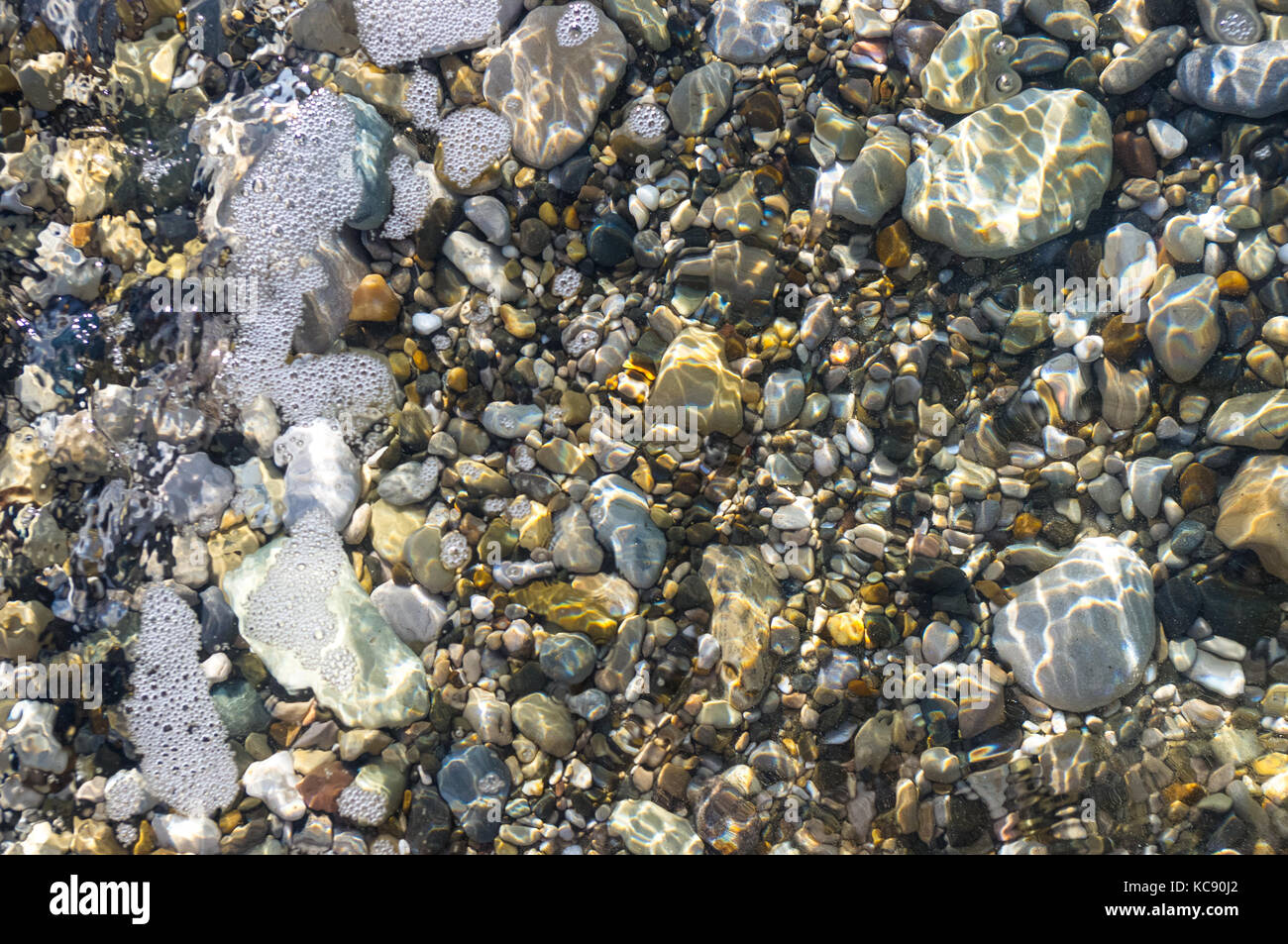 sea pebble beach with multicoloured stones, transparent waves with foam ...