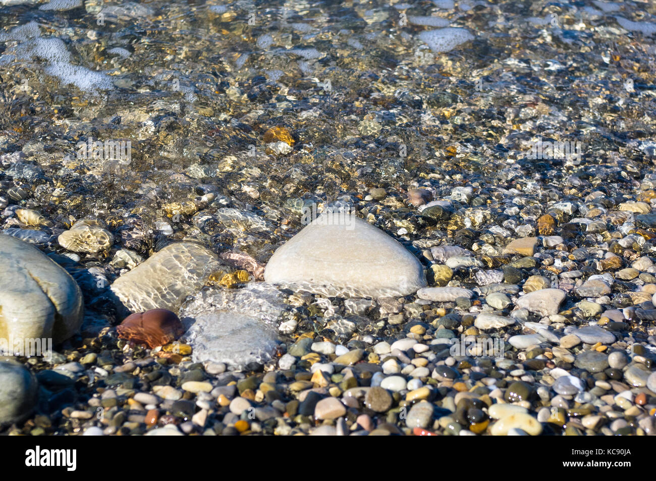 sea pebble beach with multicoloured stones, transparent waves with foam ...