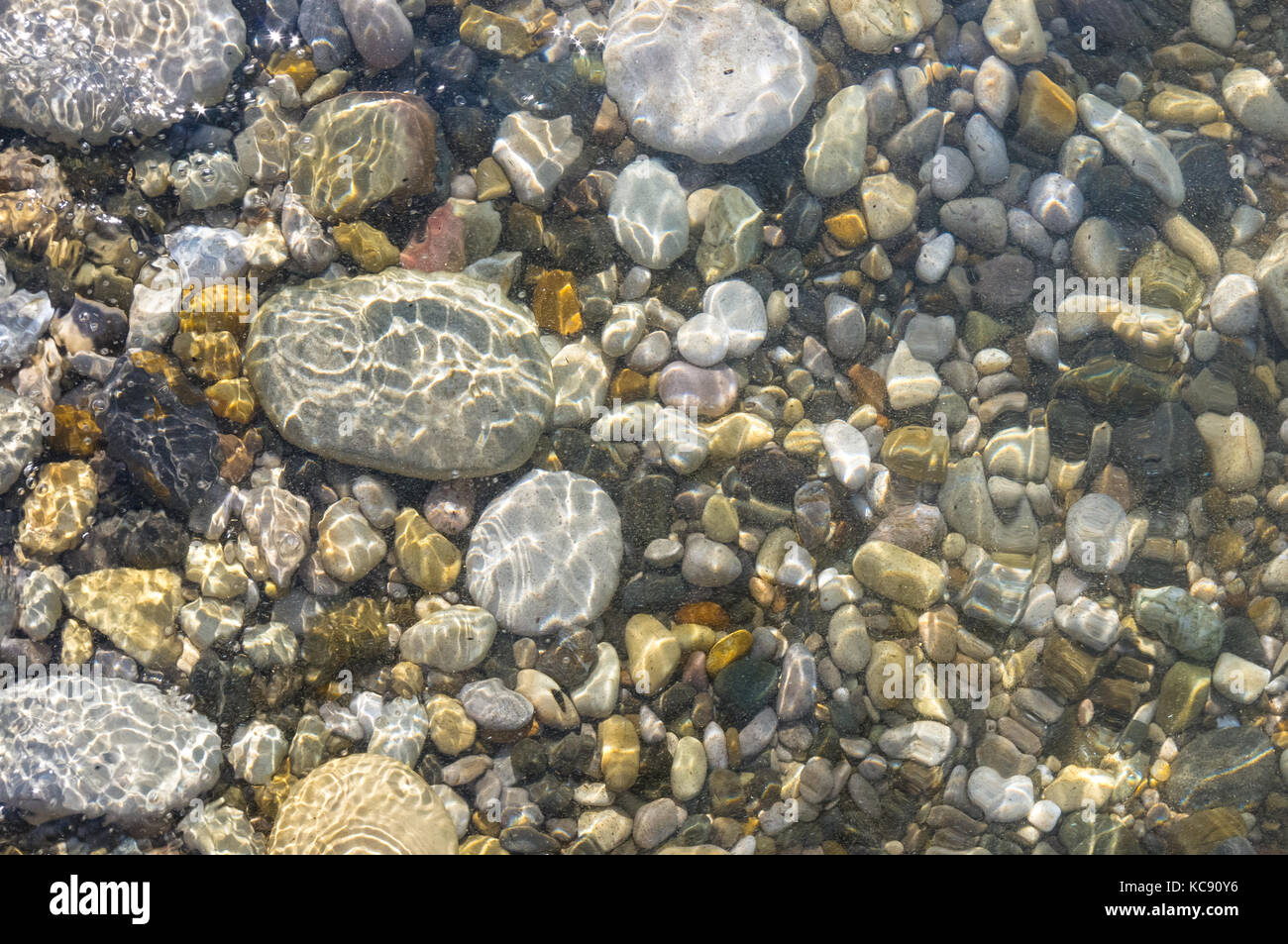 sea pebble beach with multicoloured stones, transparent waves with foam ...