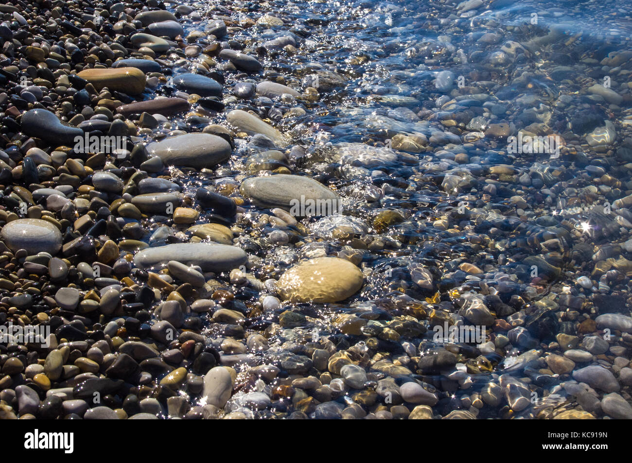 sea pebble beach with multicoloured stones, transparent waves with foam ...