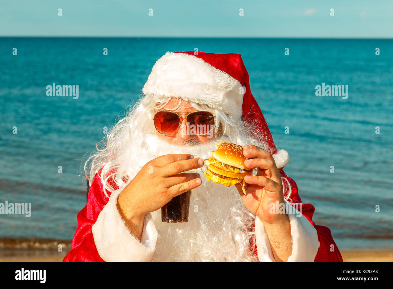 Santa Claus on the beach eating a hamburger. The concept of unhealthy ...