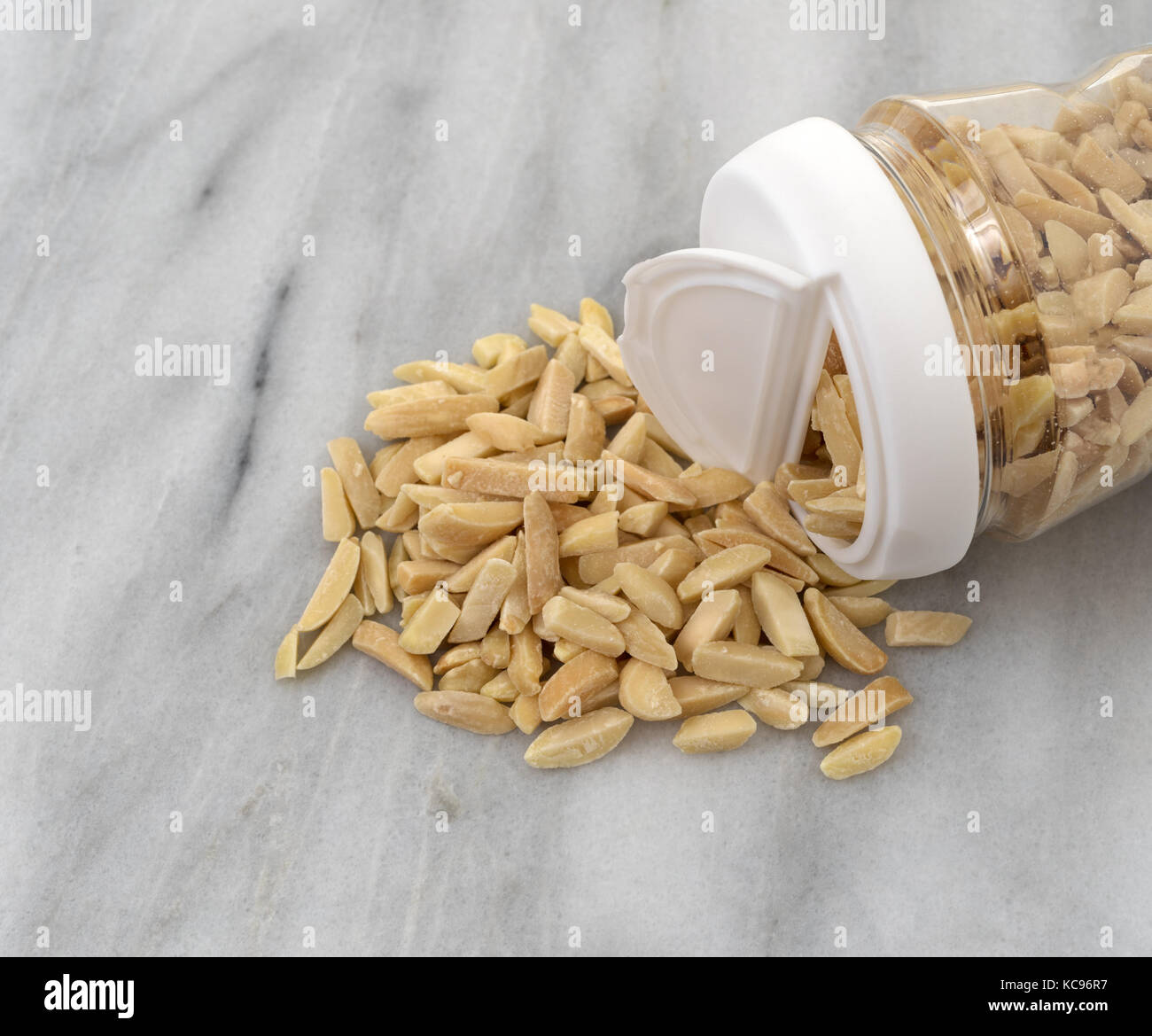 Slivered almonds spilling from a plastic container onto a marble ...