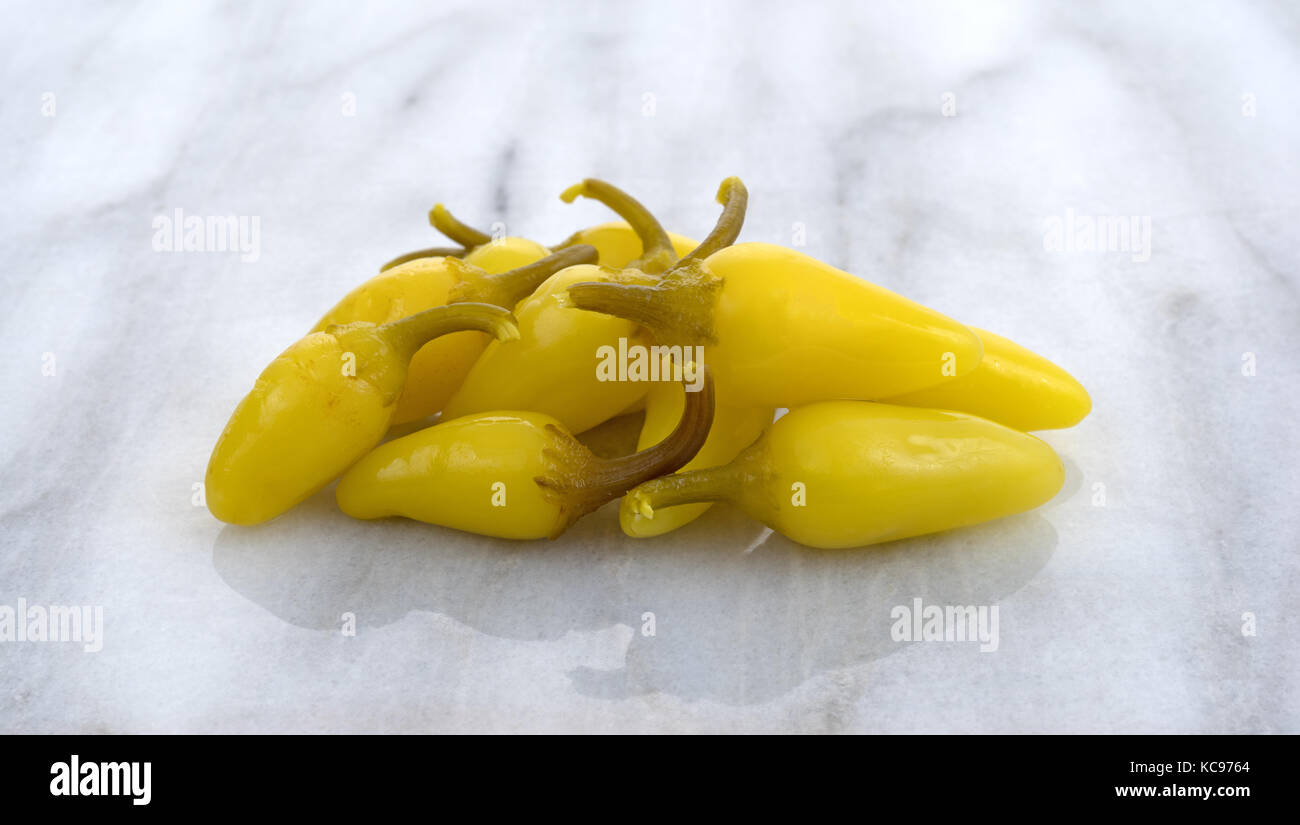 Several hot yellow canned chili peppers on a gray marble cutting board ...