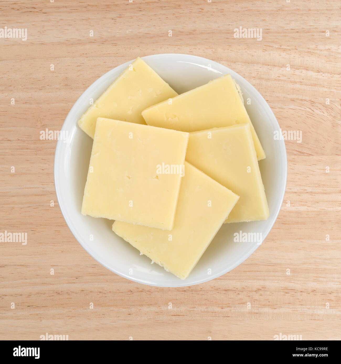 Top view of a small white bowl filled with sharp cheddar cheese square ...