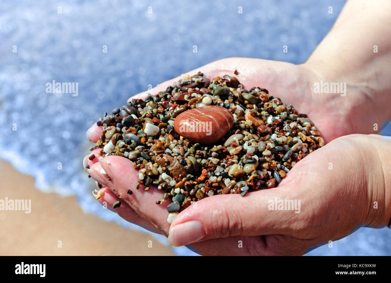 Small pabbles in hands on sea shore background Stock Photo - Alamy