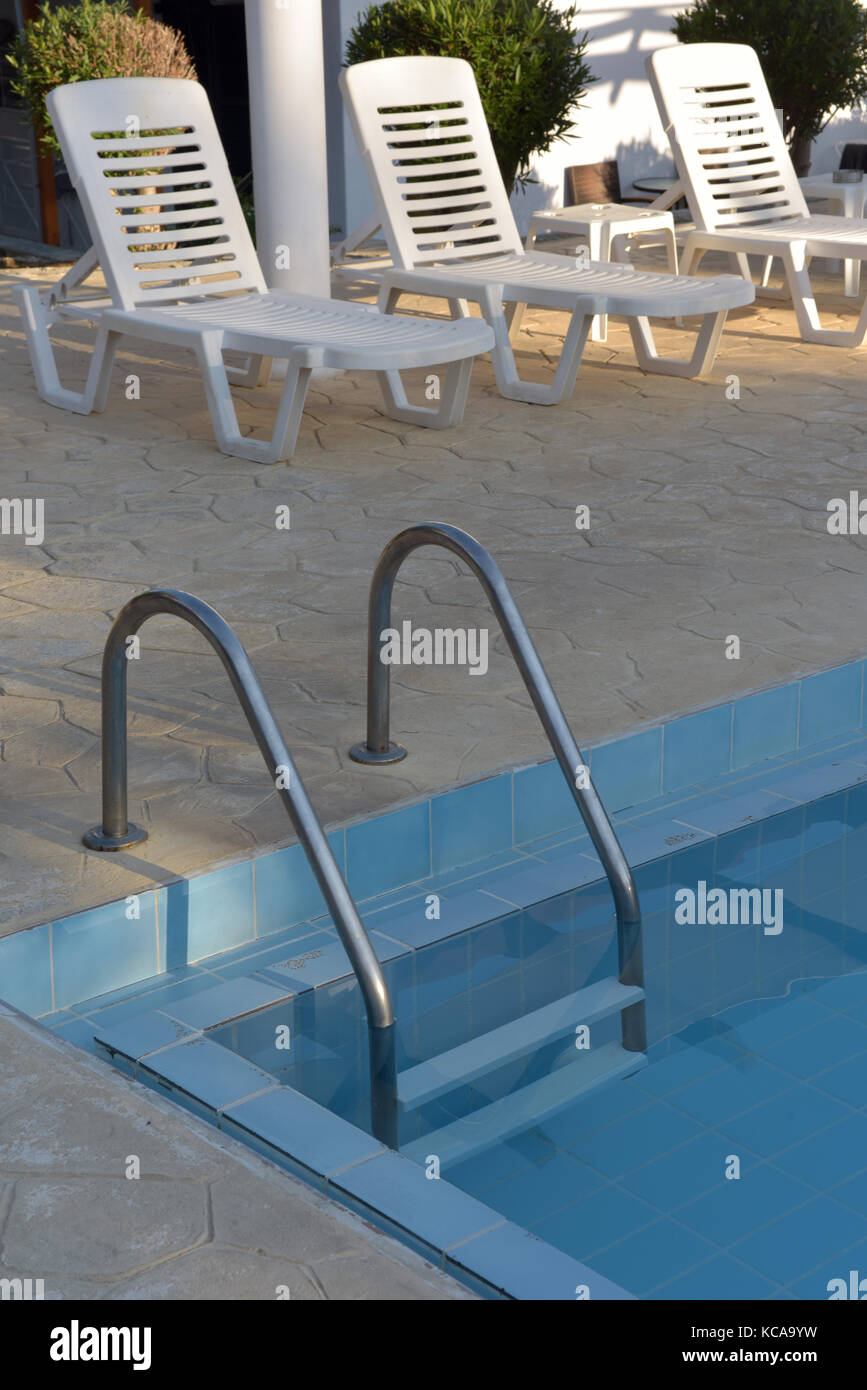 A set of steps or a ladder with handrails entering a swimming pool wih ...