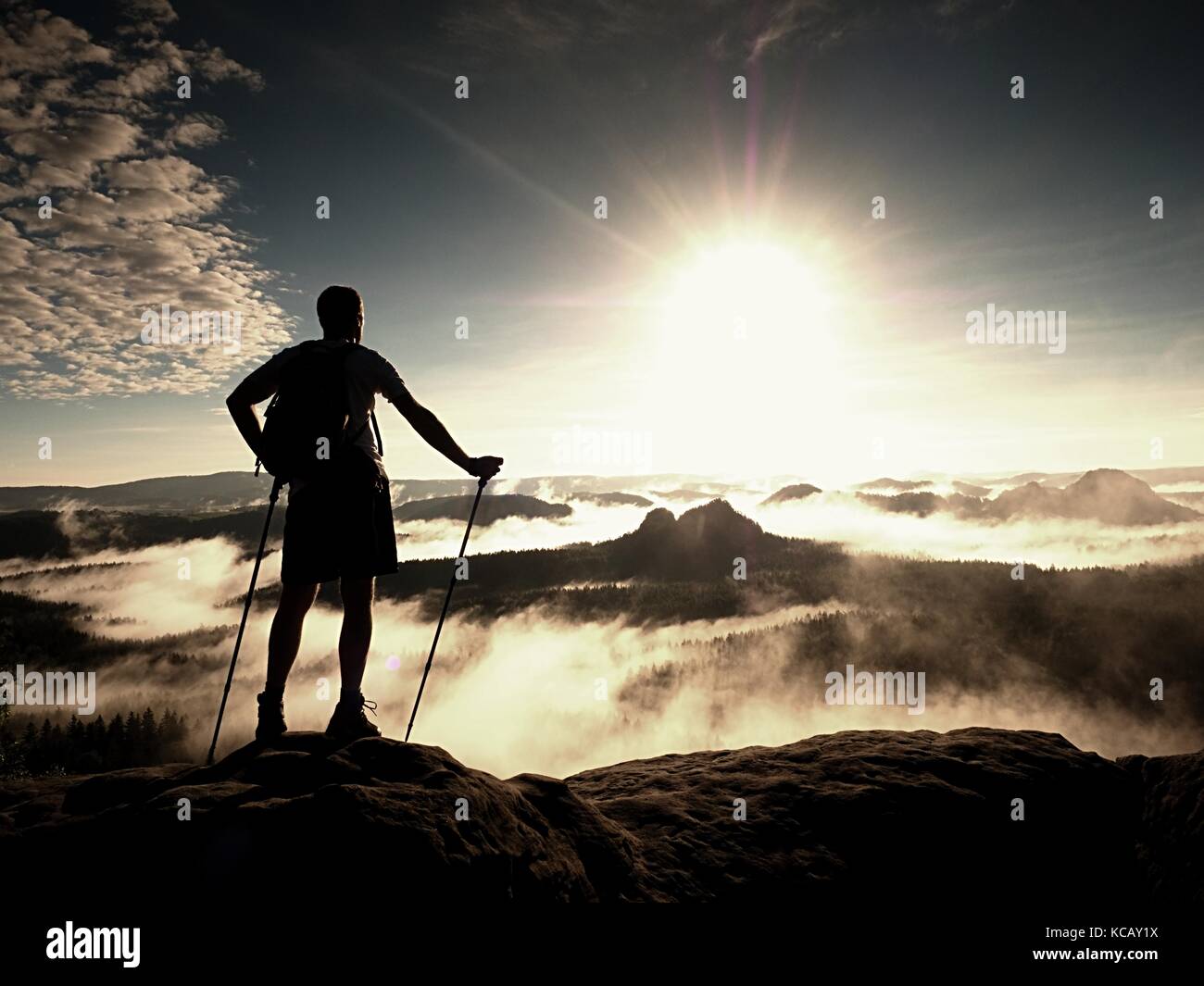 Tourist with sporty backpack and poles in hands stand on summit and ...