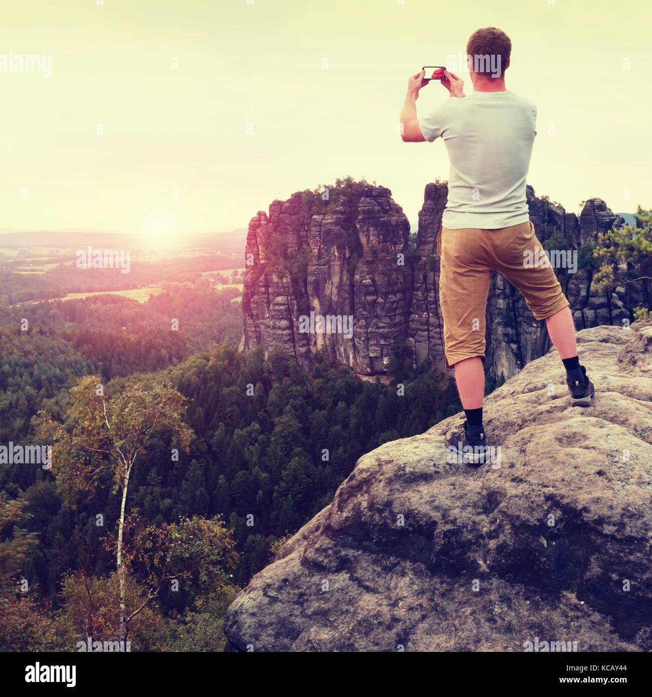 Short hair man on cliff of rock takes photo by smart phone of rocks and ...