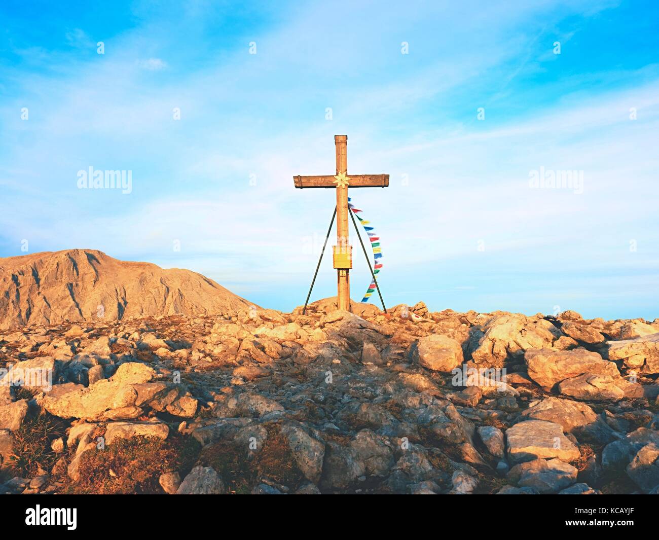 Modest wooden cross with Buddhist praying flags, raised on rocky Alpine ...
