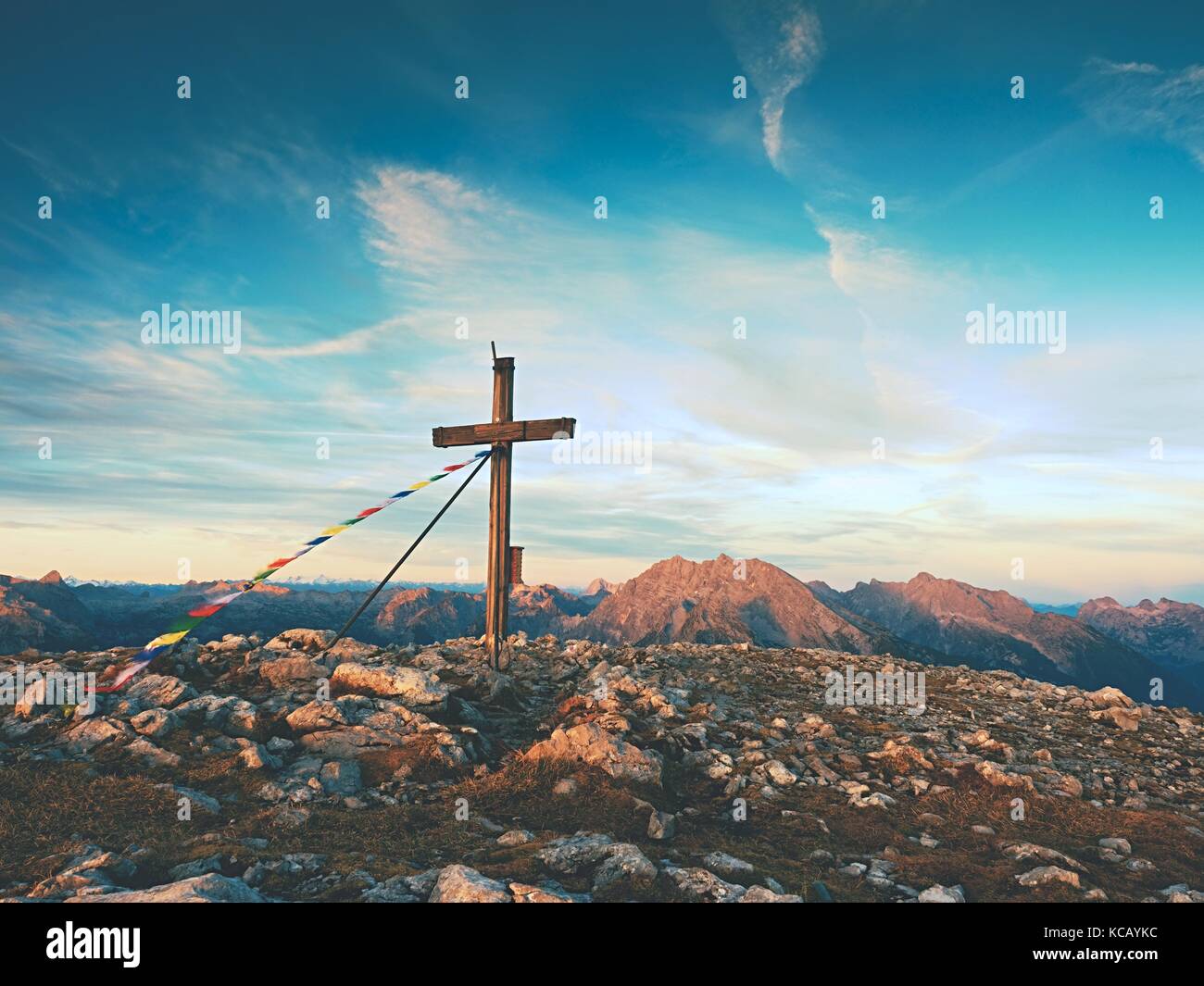 Modest wooden cross with Buddhist praying flags, raised on rocky Alpine ...