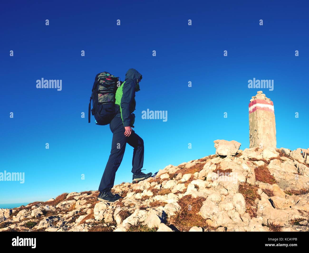 Hiker with backpack climbing on mountain peak. Summit stone at Alps ...