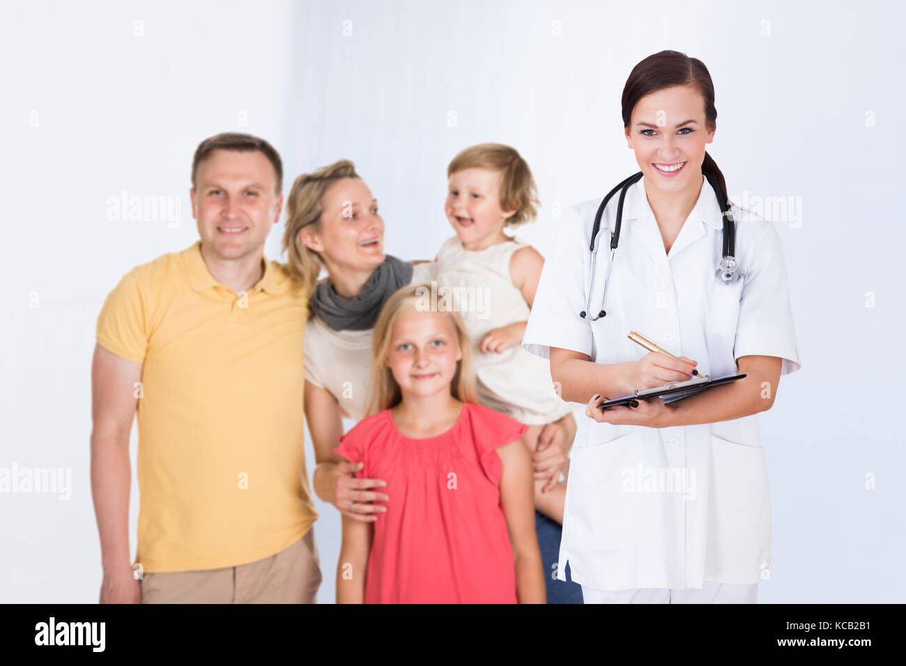 A Doctor Writing Prescription With Happy Family Standing Behind In A ...